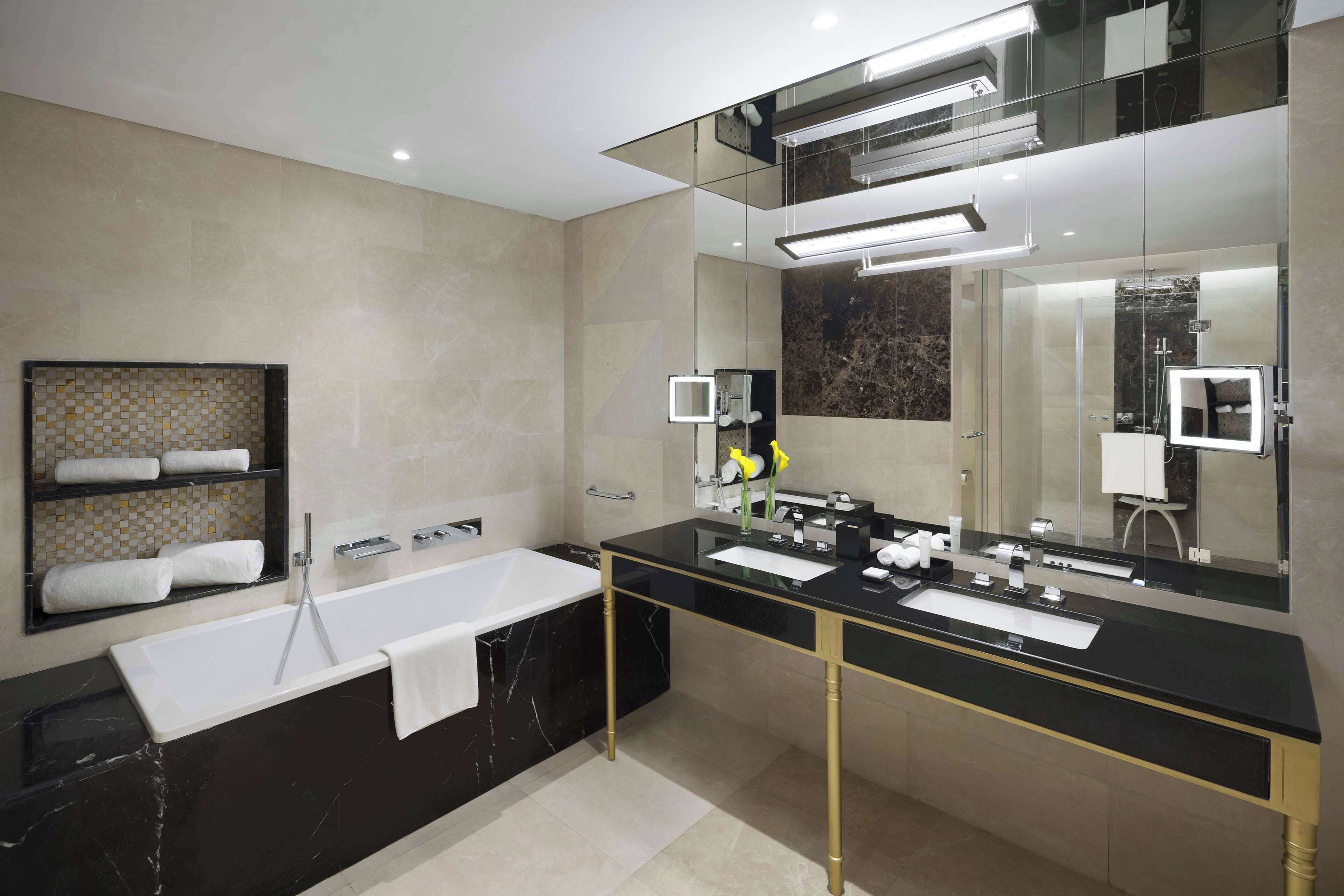 Uma casa de banho moderna com um lavatório preto e dourado, um espelho grande e uma banheira separada.