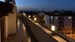 Vista noturna de uma varanda com azulejos estampados, corrimão e luminárias de rua.
