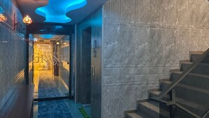 Interior moderno de hotel com uma escadaria de mármore, teto iluminado em azul e um letreiro visível 'TRAVEL LIFE'.