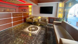 Uma área de recepção com piso de mármore, sofás de couro, uma TV de tela plana e um balcão de atendimento.