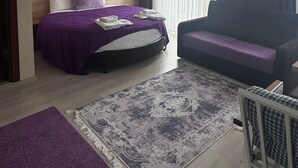 Quarto de hotel moderno com cama, sofá, tapete grande e janela com cortinas.