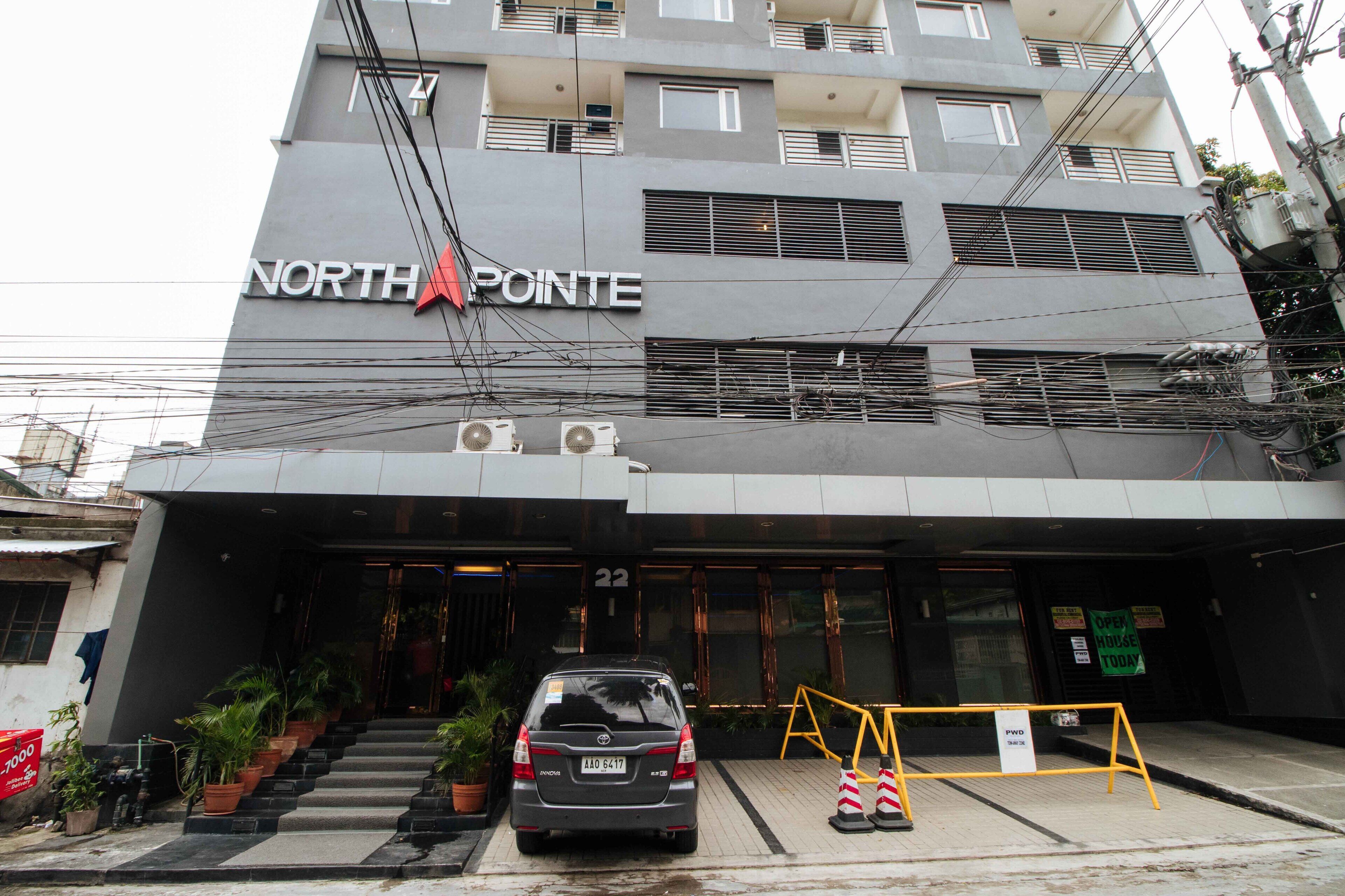 Um edifício de vários andares com a placa "NORTH PONTE" na fachada. Há unidades de ar condicionado, um carro estacionado em frente e uma barreira amarela.