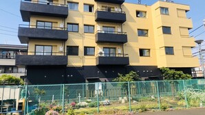 Edifício residencial com vários andares, varandas, aparelhos de ar condicionado e área de jardim murada.