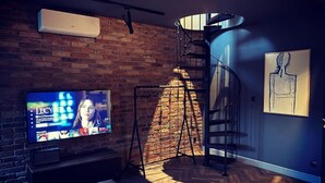 Uma sala de estar moderna com parede de tijolos, uma TV de tela plana, escada em espiral e piso de madeira.