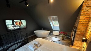 Quarto moderno com cama grande, banheira independente, televisão exibindo 'Uma Linda Mulher' e um domo de vidro.