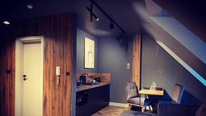 Uma sala de estar moderna com piso de madeira em padrão herringbone, um sofá cinzento, uma mesa de centro de madeira e uma área de jantar com mesa e cadeiras.