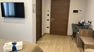 Quarto de hotel com uma cama, uma escrivaninha com cadeira, uma televisão e uma porta de madeira.