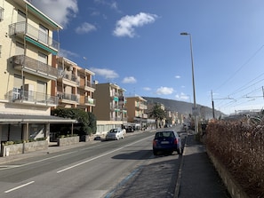 Uma rua com edifícios altos, céu claro e um carro estacionado na lateral.