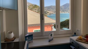 Cozinha com vista para uma vila costeira, placa indicando hóspede pela primeira vez e tábua de corte de frutas.