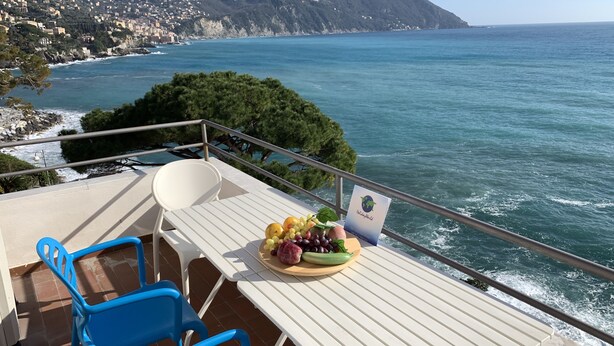 Terraço com uma mesa posta para dois, com vista para a costa e montanhas ao fundo.