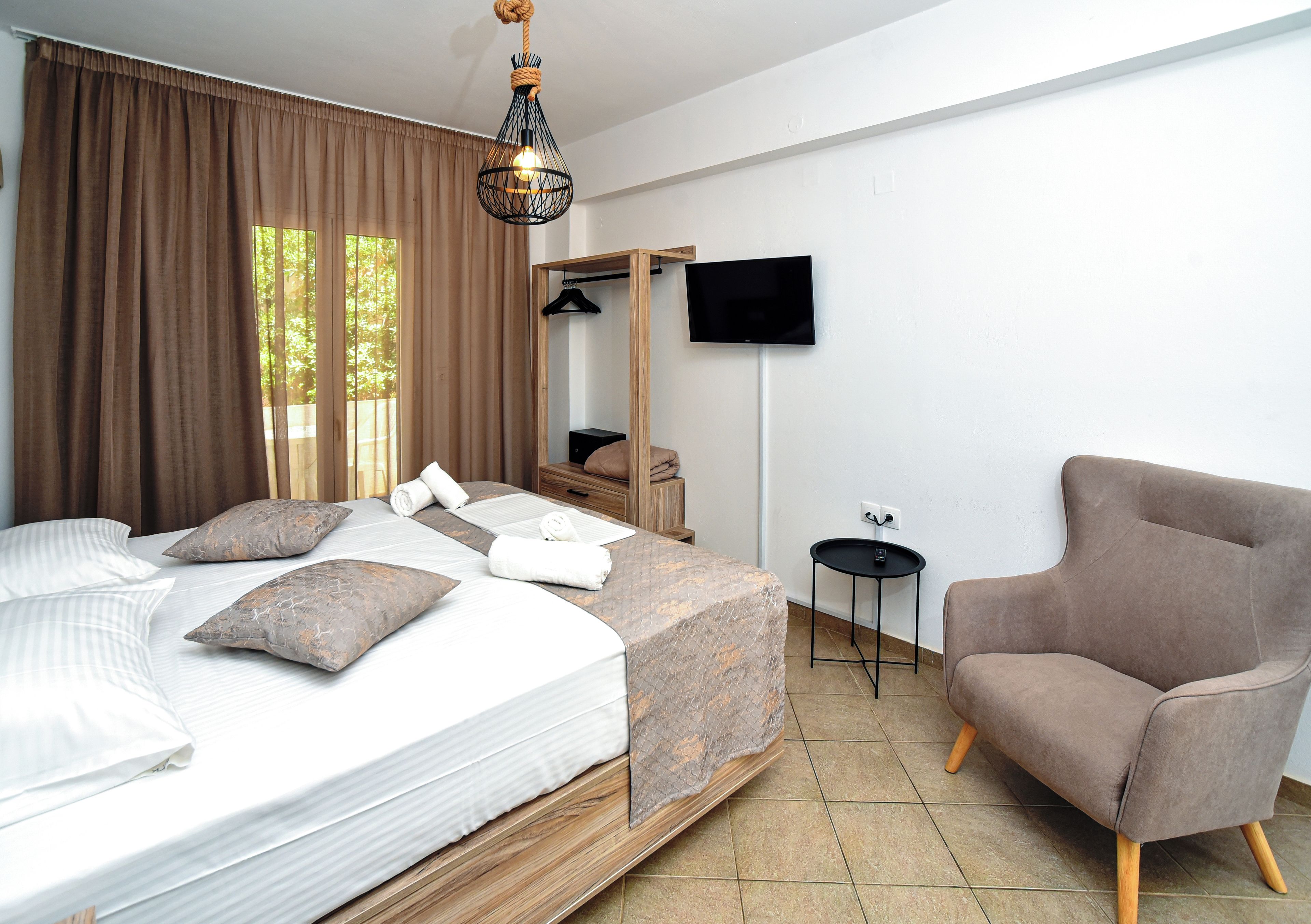 Quarto com cama, uma cadeira, televisão e janela com cortinas.