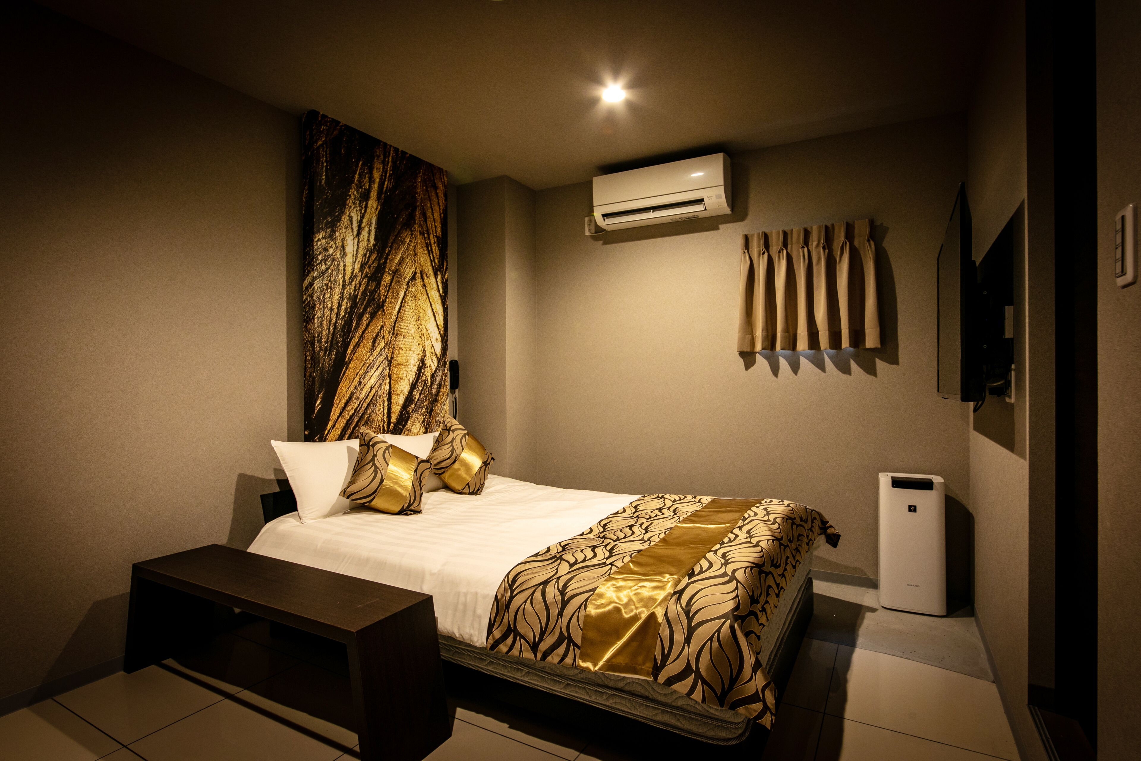 Quarto de hotel moderno com cama, mesa de cabeceira, aparelho de ar condicionado e uma grande pintura abstrata na parede.
