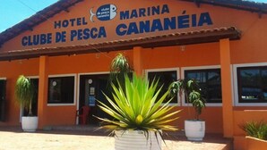 Um hotel chamado "Hotel Marina Clube de Pesca Cananeia" com uma placa, plantas em vasos e entrada com azulejos.