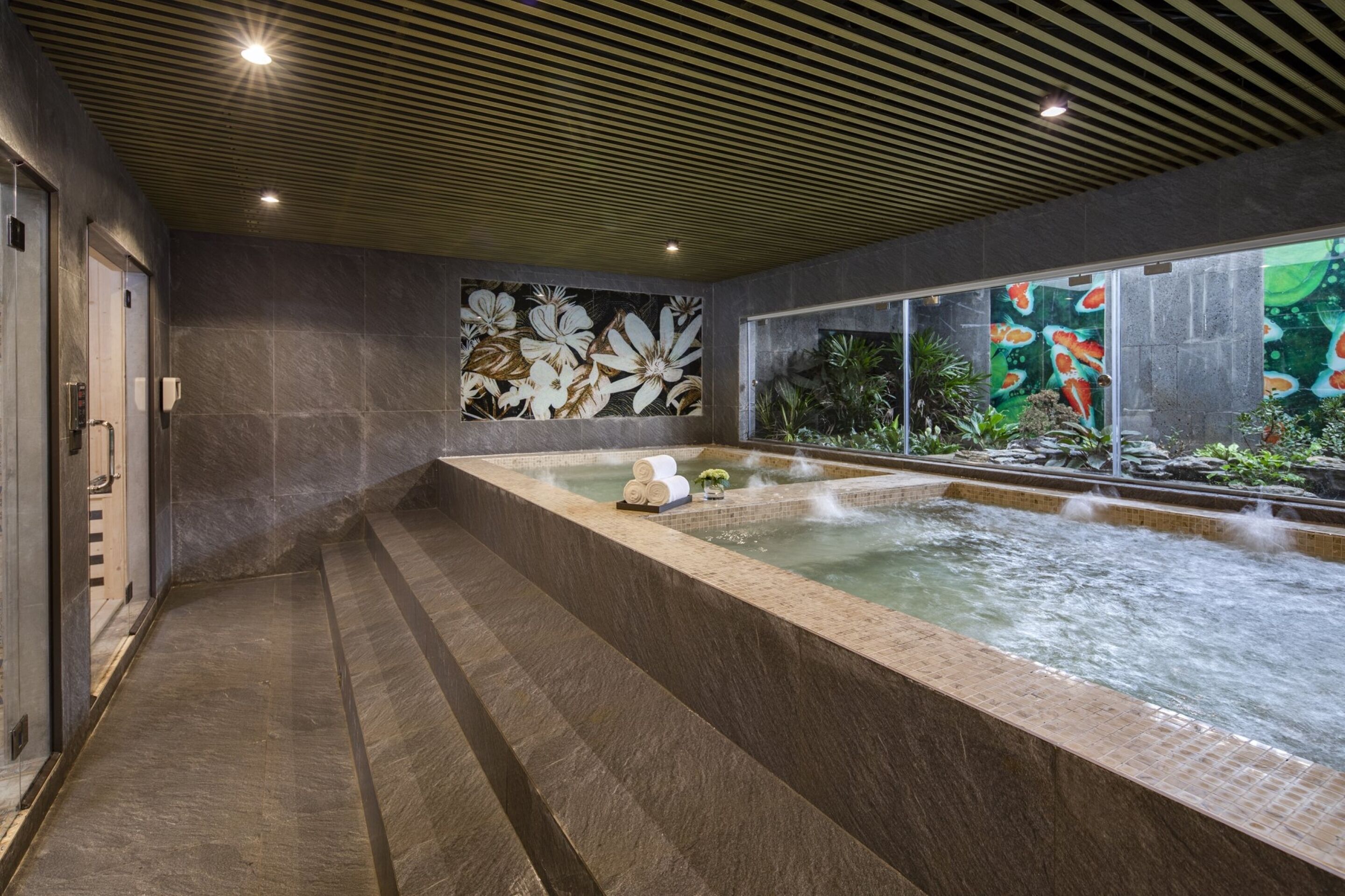 Uma área de spa com hidromassagem, paredes de pedra e um mural de flores.