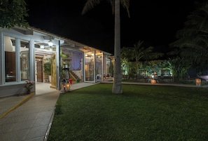 Uma casa moderna com grandes portas de vidro, um gramado bem cuidado e iluminação externa.