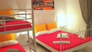 Quarto com beliches, uma cama de solteiro, um quadro de um edifício histórico, uma mesa pequena e uma cortina.