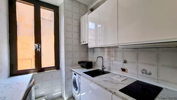 Uma cozinha moderna com armários brancos, máquina de lavar embutida, pia preta e bancada de mármore.