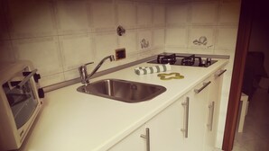 Uma cozinha com pia de aço inoxidável, fogão e armários brancos.