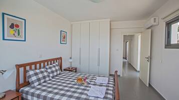 Quarto com colcha xadrez, mesa de cabeceira com abajur, quadro com legumes e guarda-roupa com portas de correr.