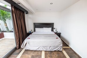Quarto de hotel moderno com uma cama grande, uma mesa de cabeceira, uma luminária e vista para o exterior.
