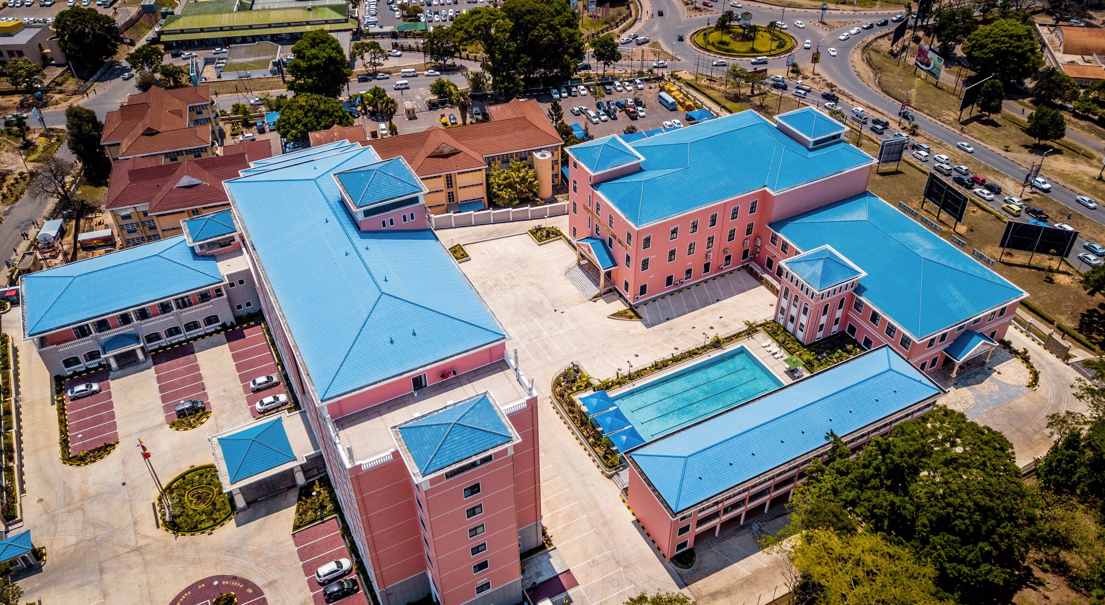 Vista aérea de um complexo hoteleiro com vários edifícios, áreas de estacionamento e uma piscina.