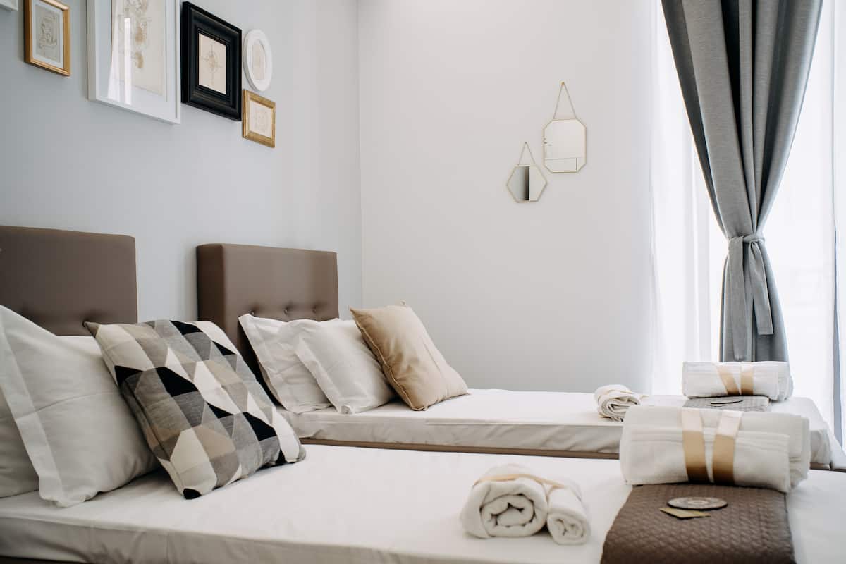 Quarto de hotel com duas camas, uma janela grande com cortinas e obras de arte fixadas na parede.