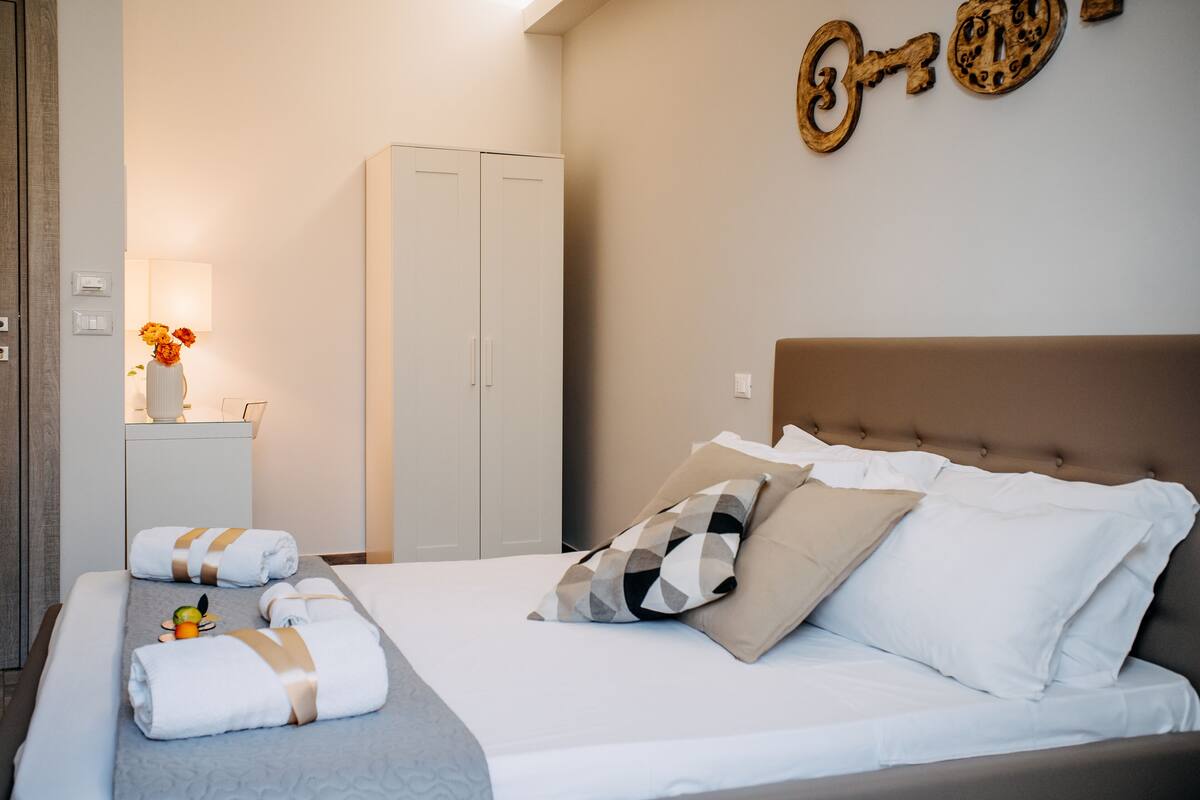 Uma cama bem arrumada com almofadas e uma toalha, um guarda-roupa e uma parede com números decorativos.
