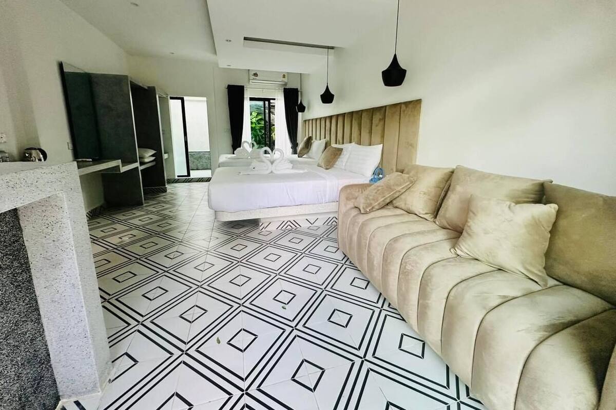 Quarto de hotel moderno com piso estampado, uma cama grande, um sofá bege e uma televisão.