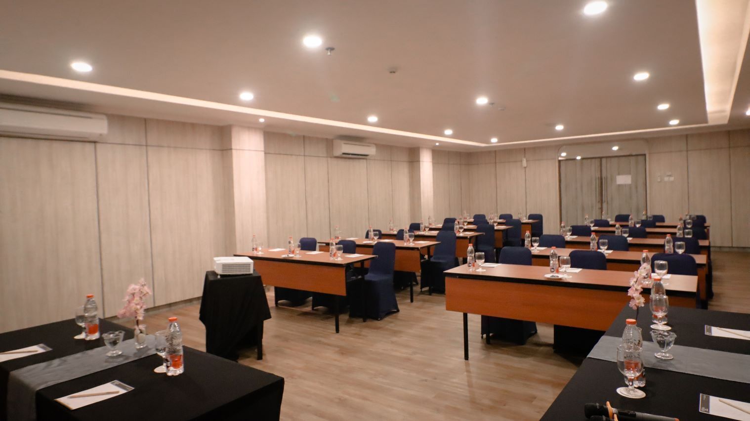Uma sala de conferências com várias mesas, cadeiras e um projetor.