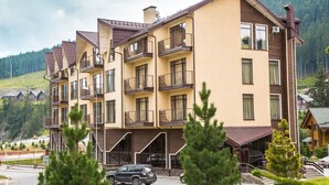 Um hotel com vários andares, varandas, área de estacionamento e montanhas ao fundo.