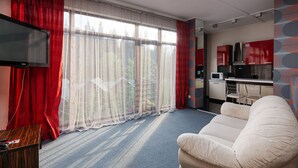 Quarto de hotel moderno com uma janela grande, televisão de tela plana, sofá e cozinha compacta.