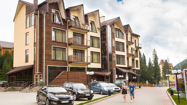 Um edifício com vários andares, varandas, área de estacionamento e calçada pavimentada.