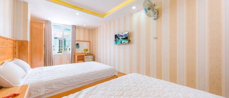 Quarto de hotel com duas camas, uma cabeceira de madeira, mesa de cabeceira, televisão e janela com cortinas.