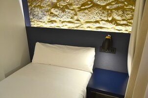 Uma cama de solteiro com travesseiro branco e cabeceira, com parede texturizada ao fundo.