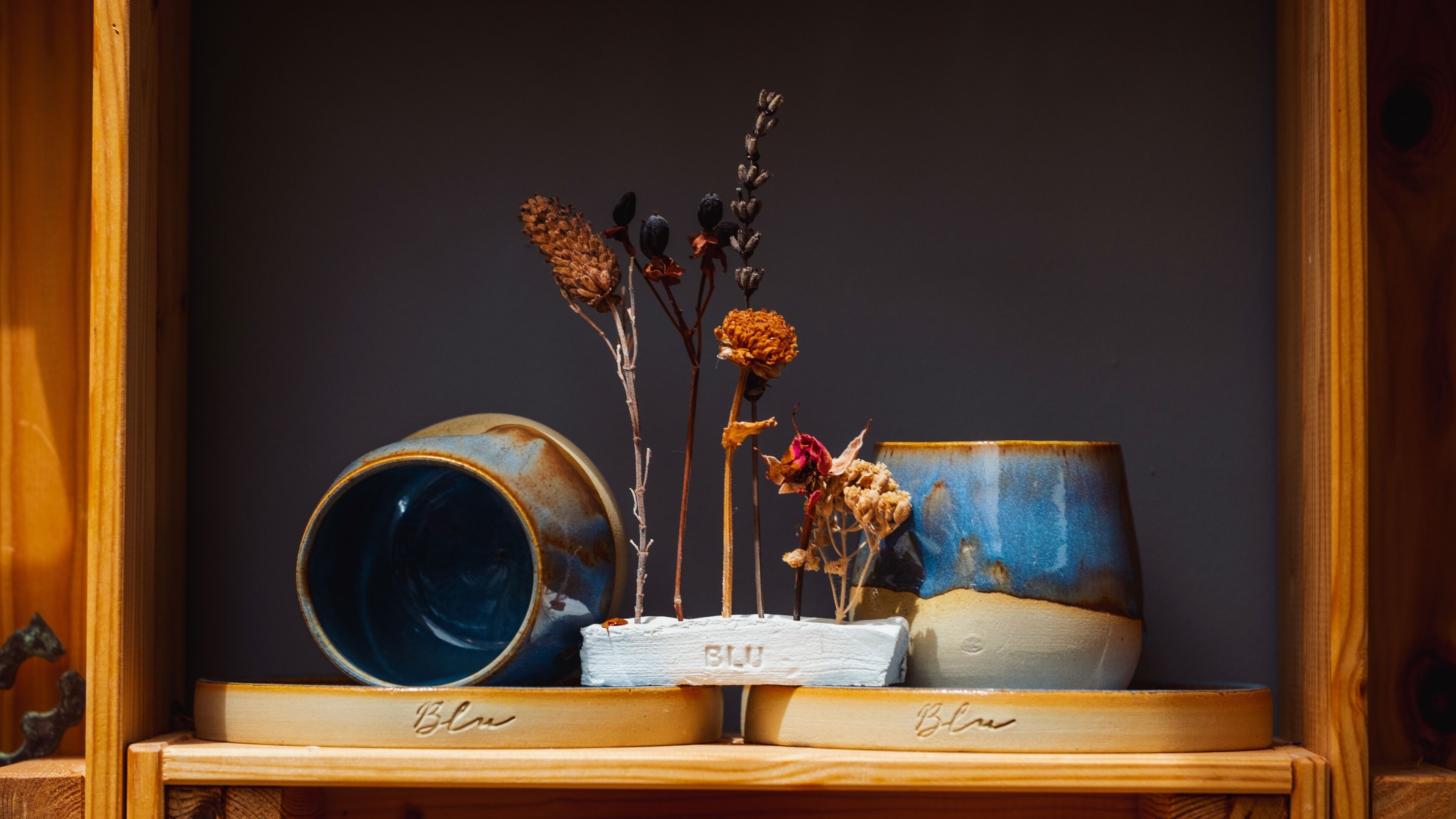 Um armário de madeira com duas tigelas de cerâmica e um vaso com flores secas.