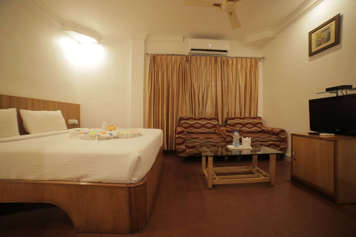 Quarto de hotel com cama, sofá, televisão e ar condicionado.