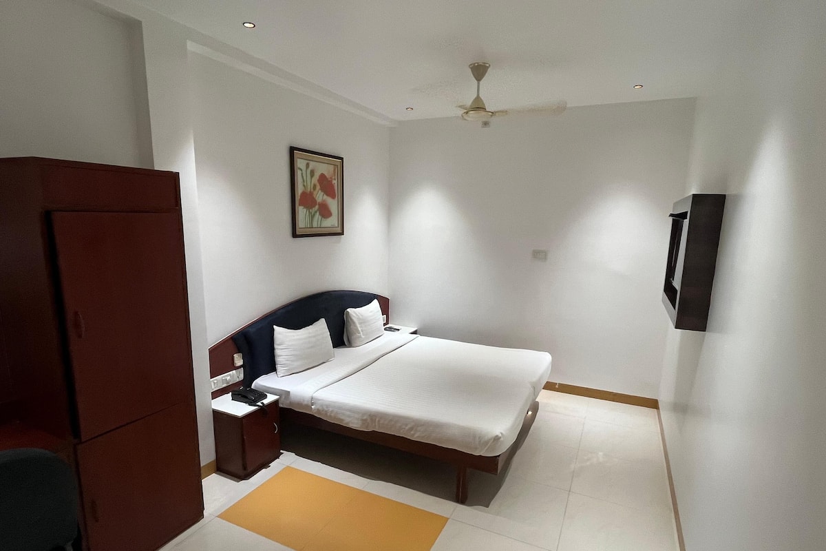 Quarto de hotel com cama, guarda-roupa, escrivaninha com telefone, pintura na parede e ventoinha no teto.