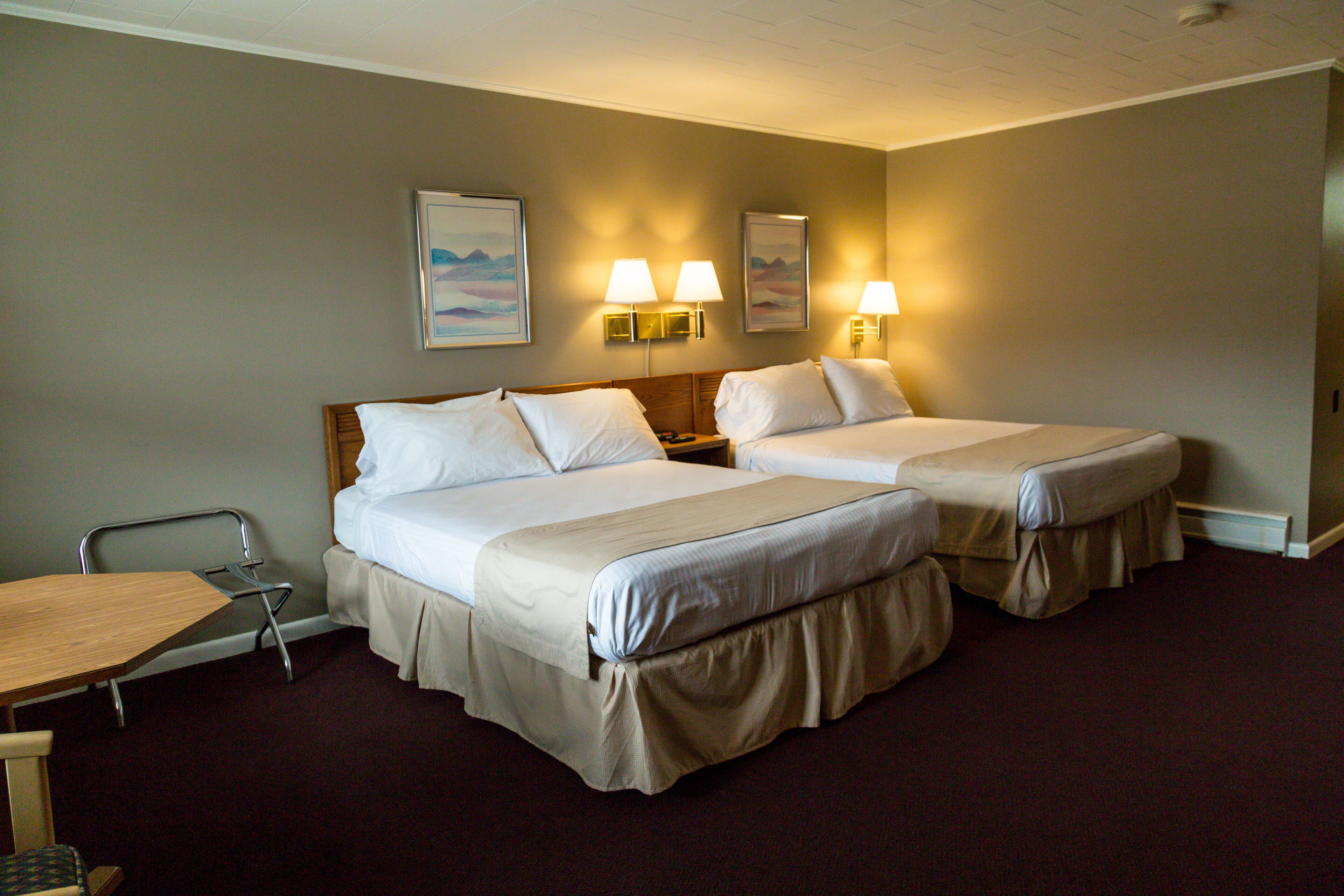 Quarto de hotel com duas camas, uma escrivaninha e duas luminárias.