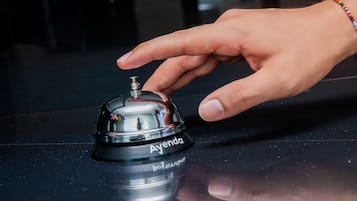 Uma mão pressionando um sino de hotel com o nome 'Ayenda'.