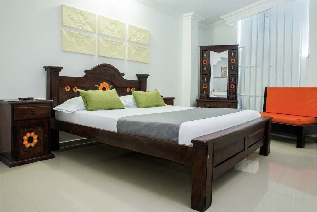 Quarto com cama de madeira, duas mesas de cabeceira, um espelho e uma cadeira laranja.
