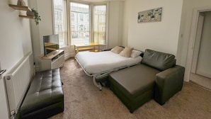 Quarto compacto com cama, escrivaninha pequena, cadeira, sofá e radiador.