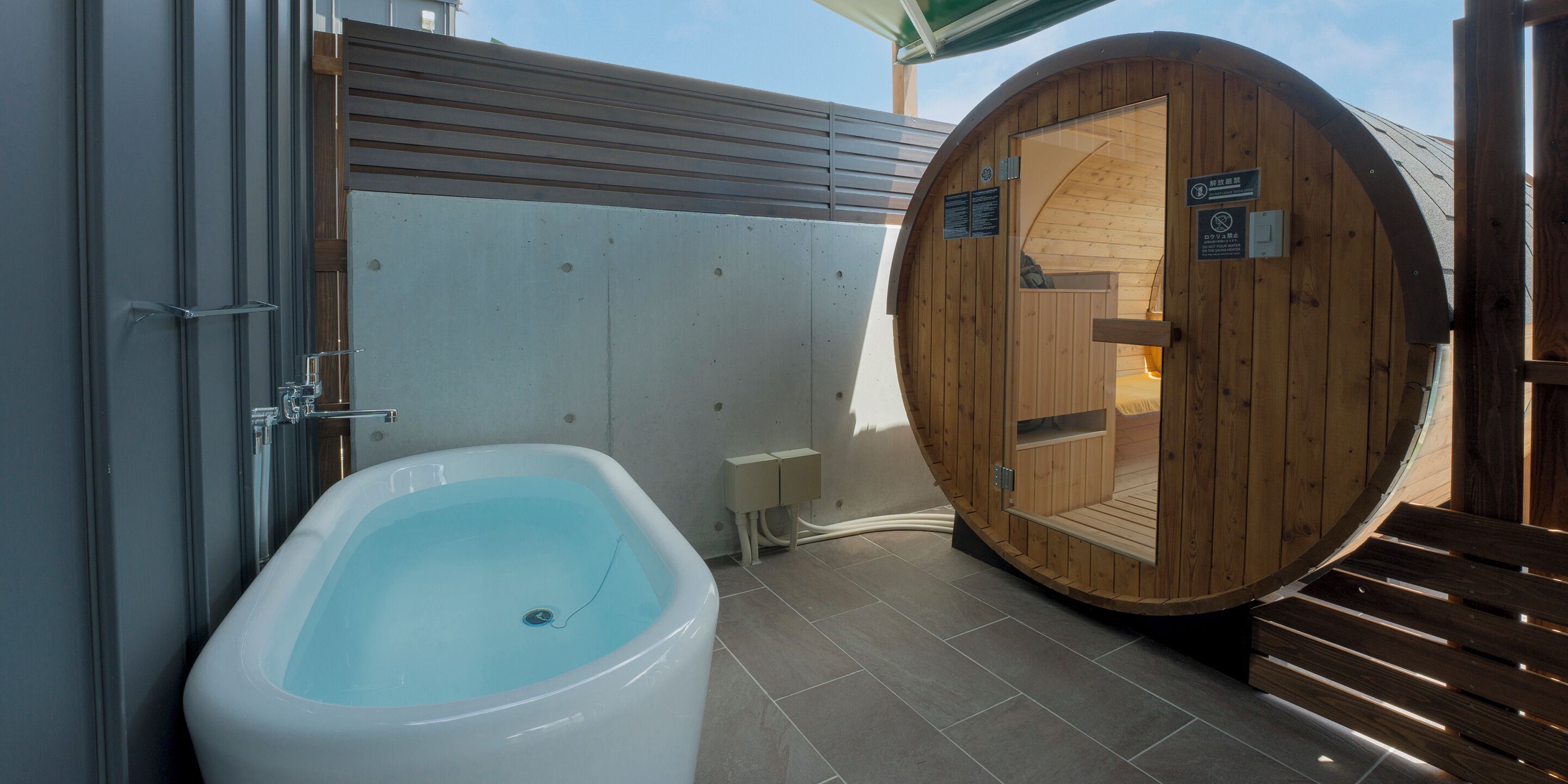 Uma sauna com porta de madeira, banheira branca e chão ladrilhado.