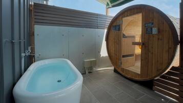 Uma sauna com porta de madeira, banheira branca e chão ladrilhado.