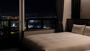 Quarto de hotel com cama, janela com cortinas e vista para a paisagem urbana noturna.