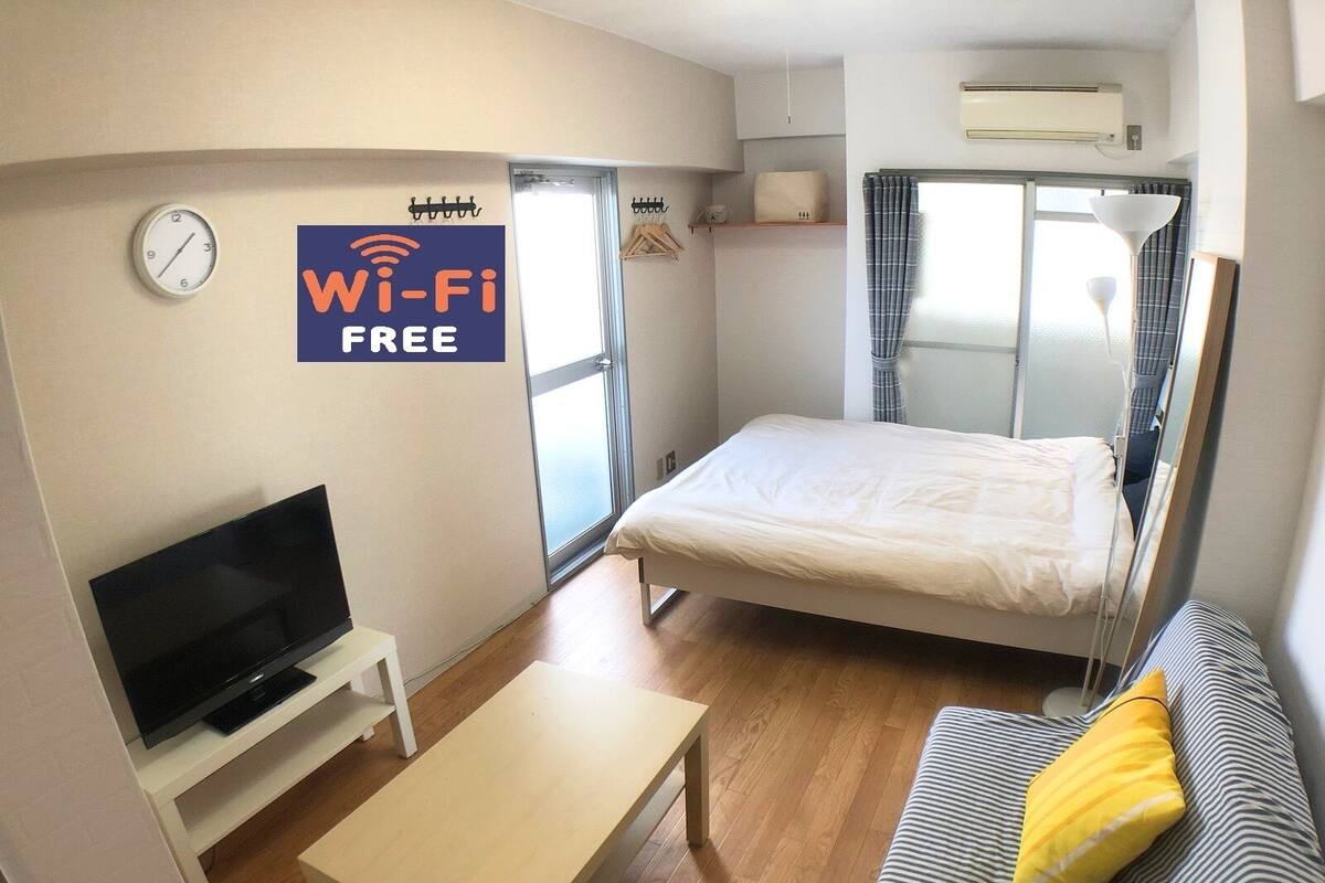 Quarto com cama, televisão, sofá, mesa pequena e placa indicando Wi-Fi gratuito.