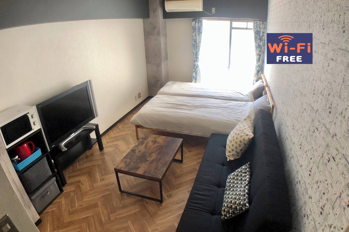 Quarto compacto com cama, sofá, televisão e uma pequena mesa.