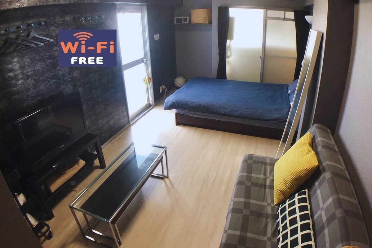 Quarto moderno com cama, sofá, televisão e símbolo de Wi-Fi indicando acesso gratuito.