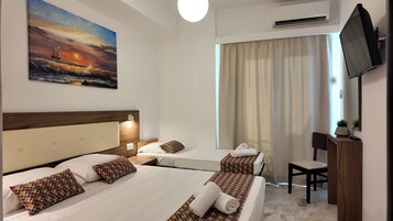Quarto de hotel com duas camas, televisão, escrivaninha e pintura de um pôr do sol sobre o oceano.