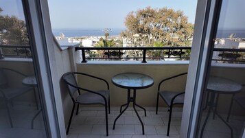 Varanda com duas cadeiras e uma mesa pequena, com vista para o mar e edifícios.