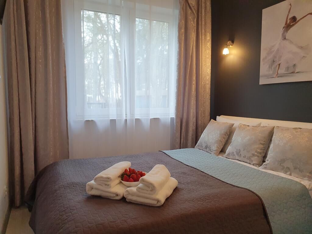 Uma cama bem arrumada com toalhas dobradas e uma tigela de morangos, um quadro na parede e uma janela com cortinas.